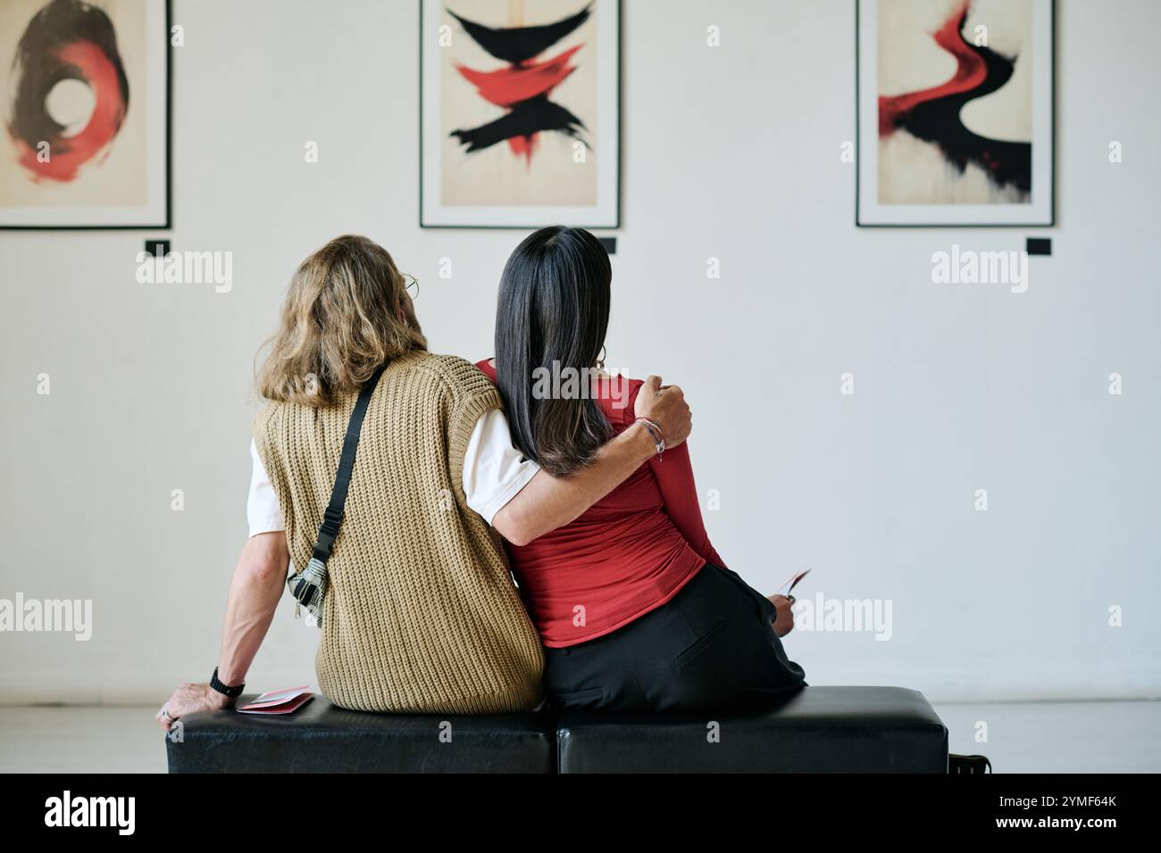 Two women sitting on black bench, admiring abstract paintings on ...