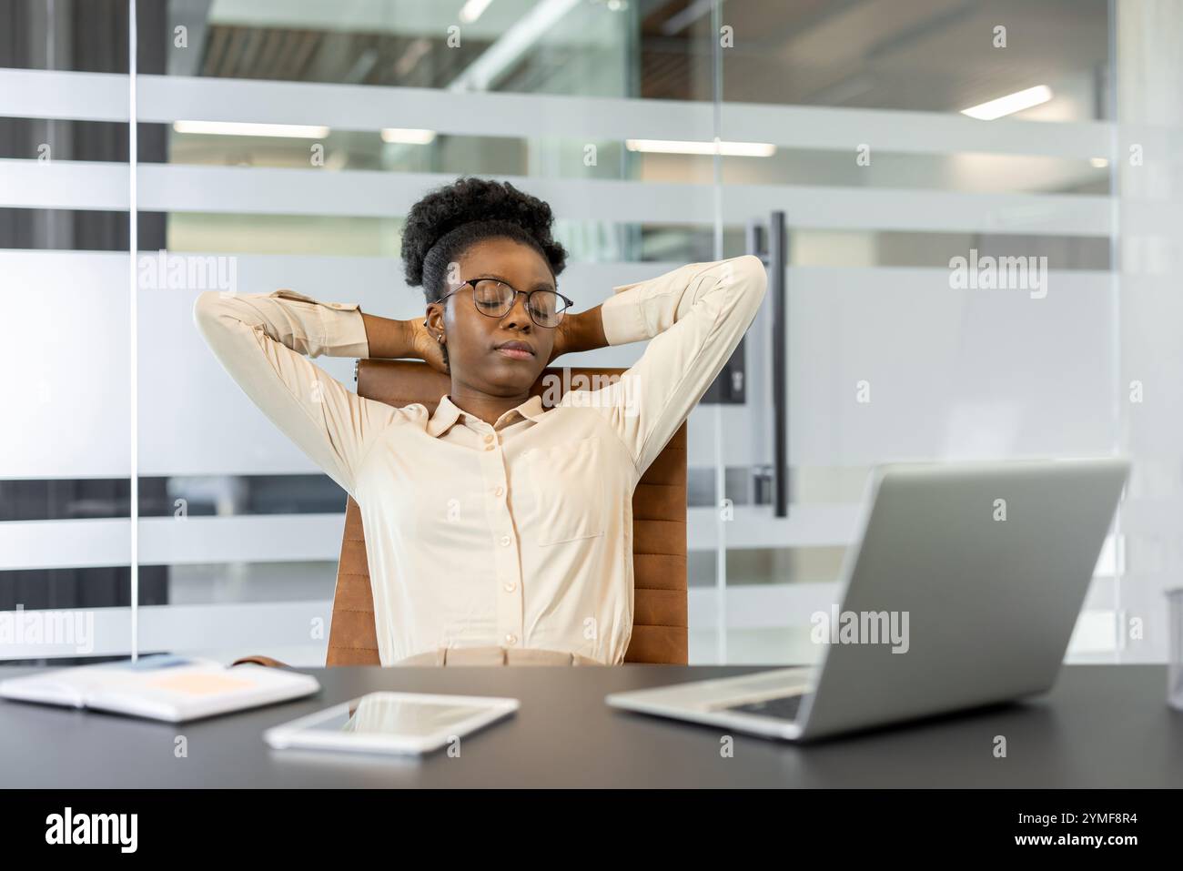Businesswoman relaxing at office desk with closed eyes, hands behind ...