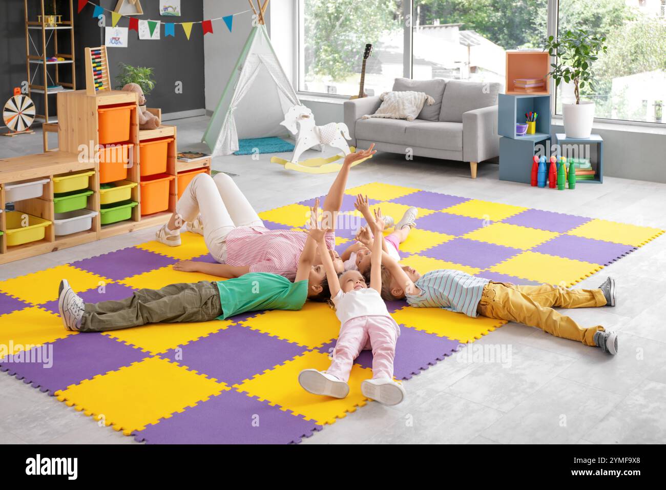 Little children with nursery teacher lying on floor in kindergarten ...