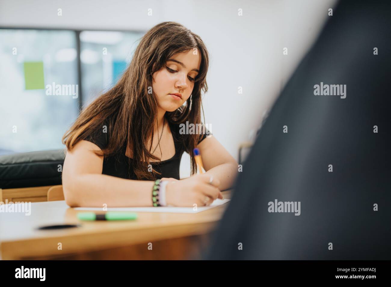 Focused high school student writing in classroom during school day ...