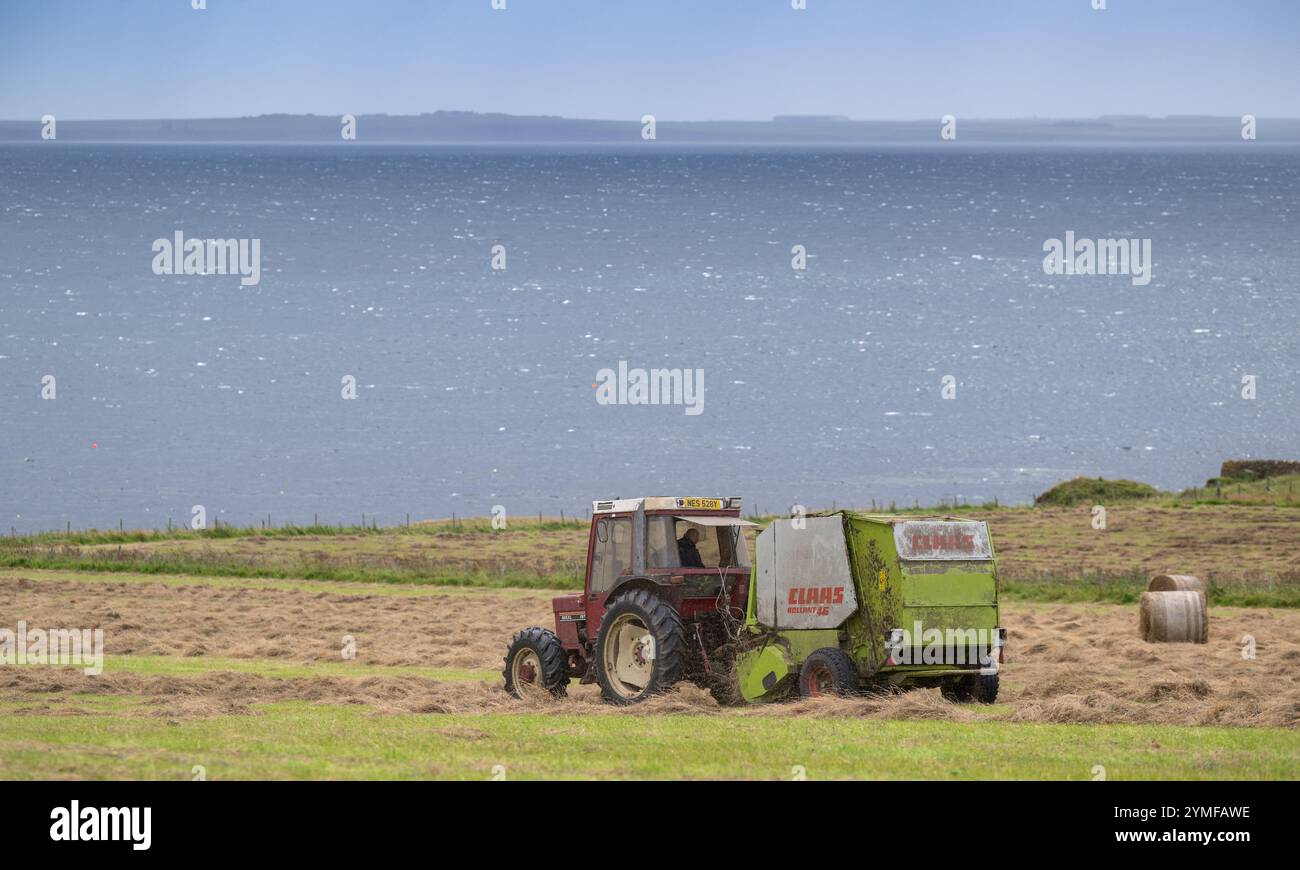 Farmer baling round bales of hay with a vintage International tractor ...