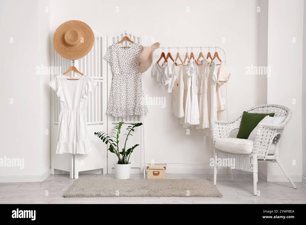 Rack with stylish female clothes, hats, wicker armchair and houseplant ...