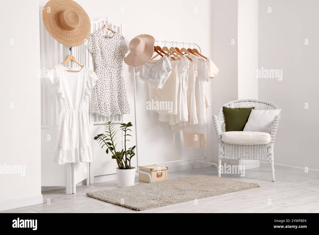 Rack with stylish female clothes, hats, wicker armchair and houseplant ...