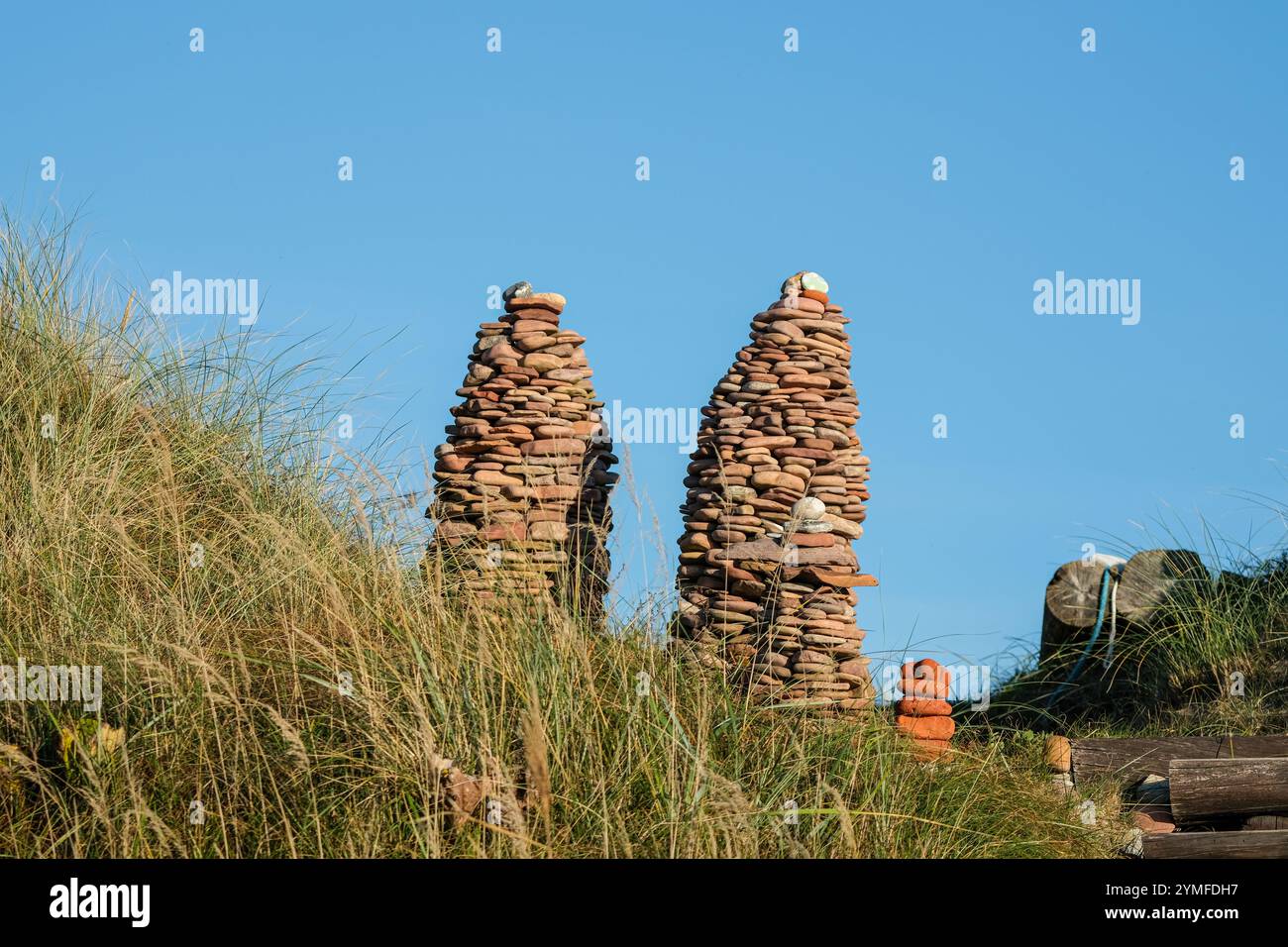 Two tall pebble towers stand amidst grassy dunes under a clear blue sky ...