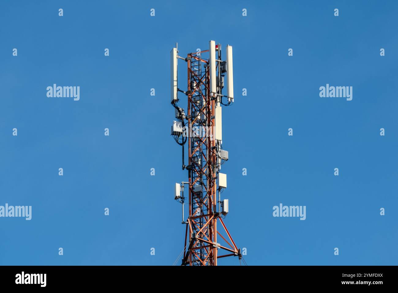 A telecommunications cell tower with antennas and equipment, set against a clear blue sky ...