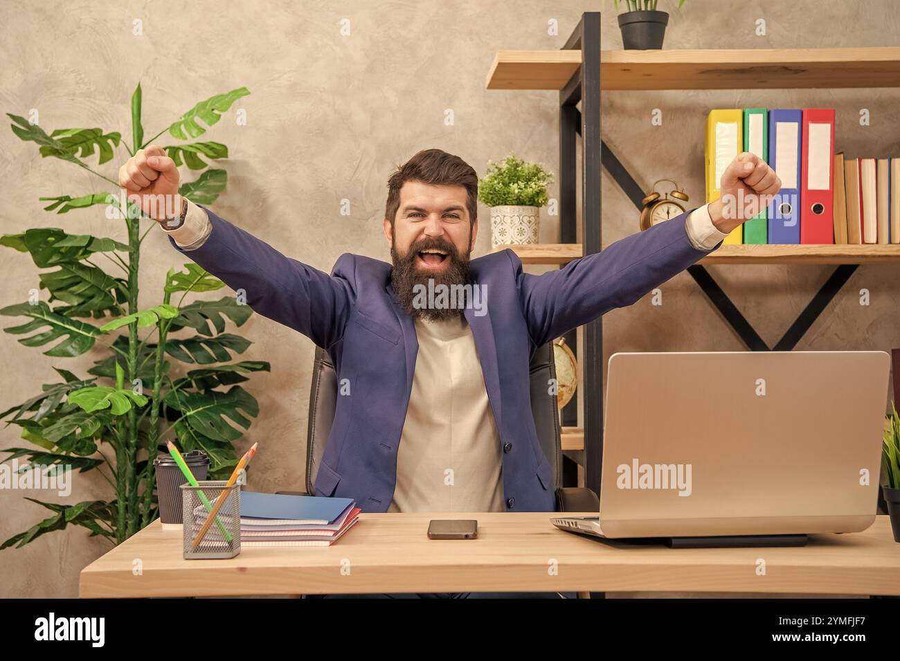 Happy businessman making winning gesture working at office desk, win ...