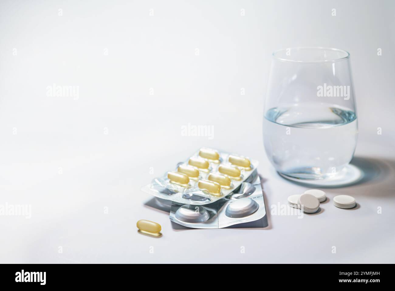 Pills and capsules separately and in blister packs next to a glass with ...