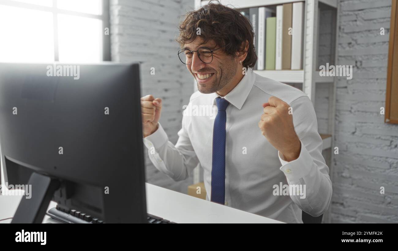Young man celebrating success at office desk in modern workplace with ...