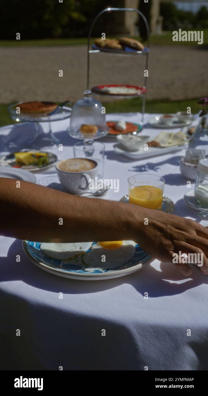 Outdoor breakfast setting featuring a woman's arm reaching for juice on ...