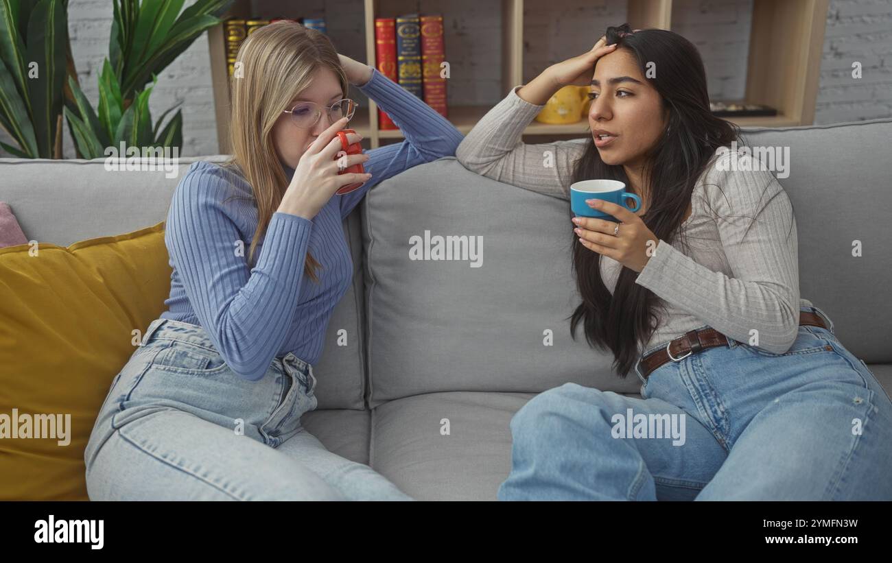 Two women friends having a serious conversation on a grey couch indoors ...