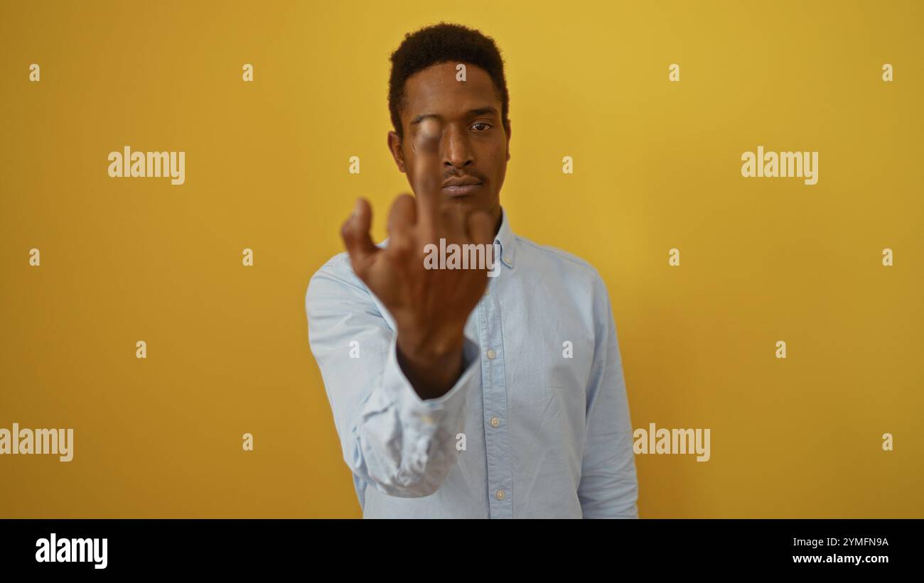 Young man making a gesture while standing against a vibrant yellow ...