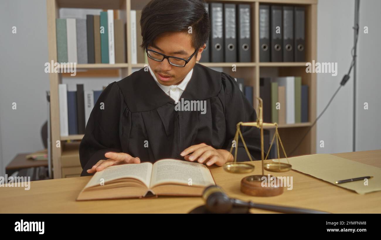 Young, chinese man in a judge's robe reading a book in an office with ...