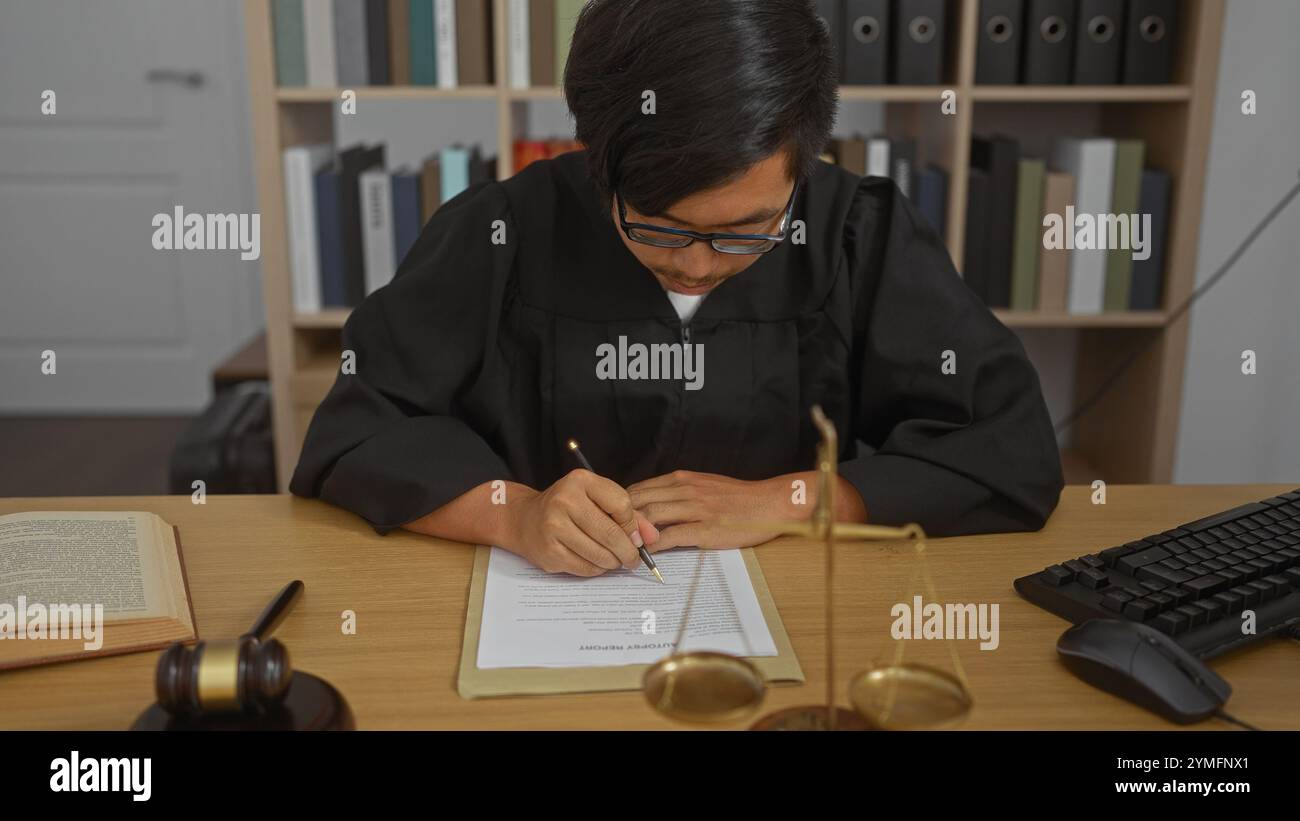 Young man in judge's robe writing at desk in office with scales of ...