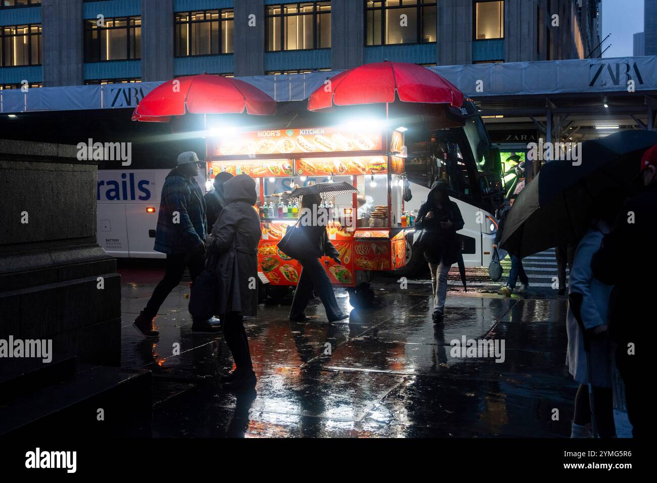 People walk through rainfall using umbrellas past a food cart, Thursday ...
