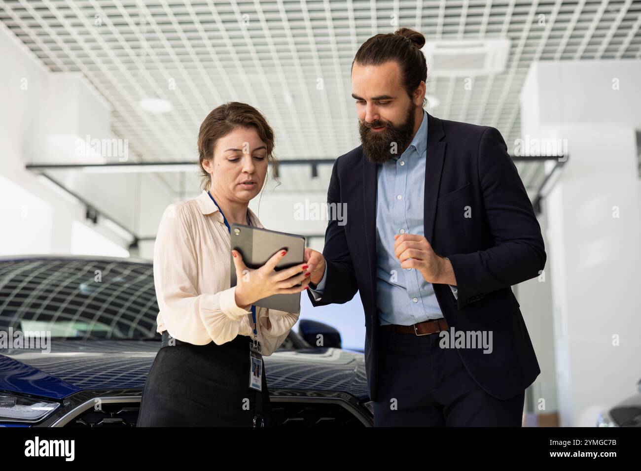 Car dealership saleswoman reading text on tablet to man, providing information about available ...