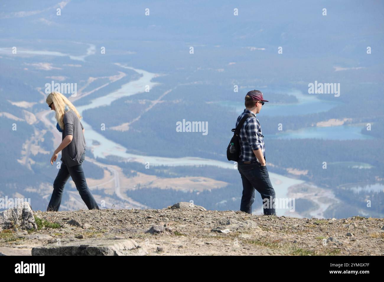 two people on mountain top look over distant view of river valley and ...