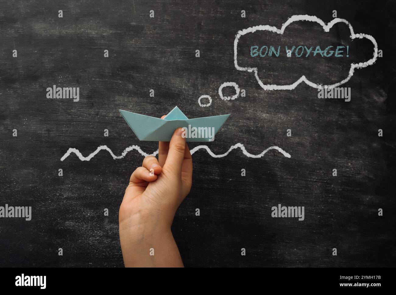 A hand holding a paper boat in a chalkboard with the words Bon Voyage ...
