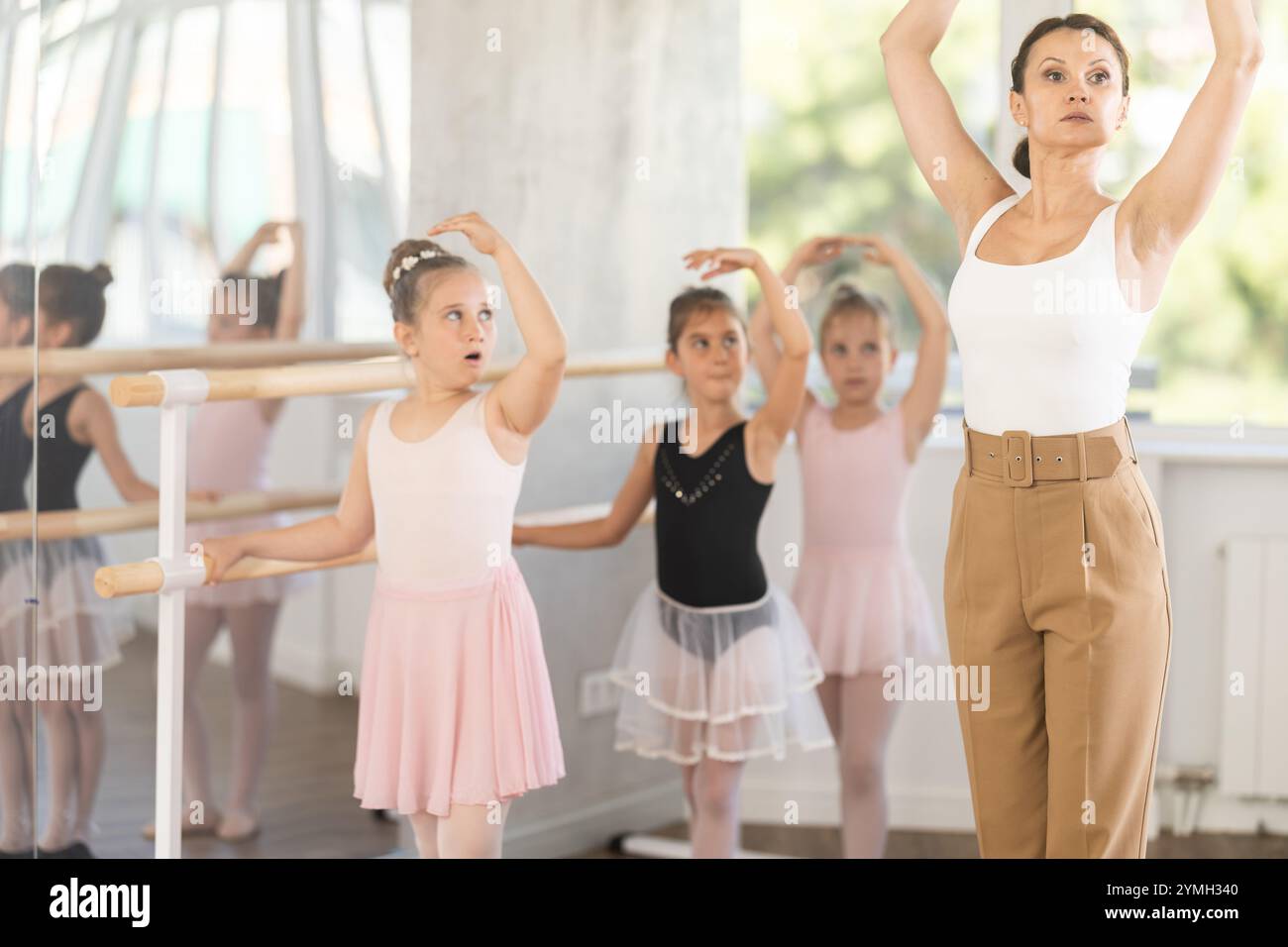 Girl students of choreographic school look at woman teacher and repeat ...