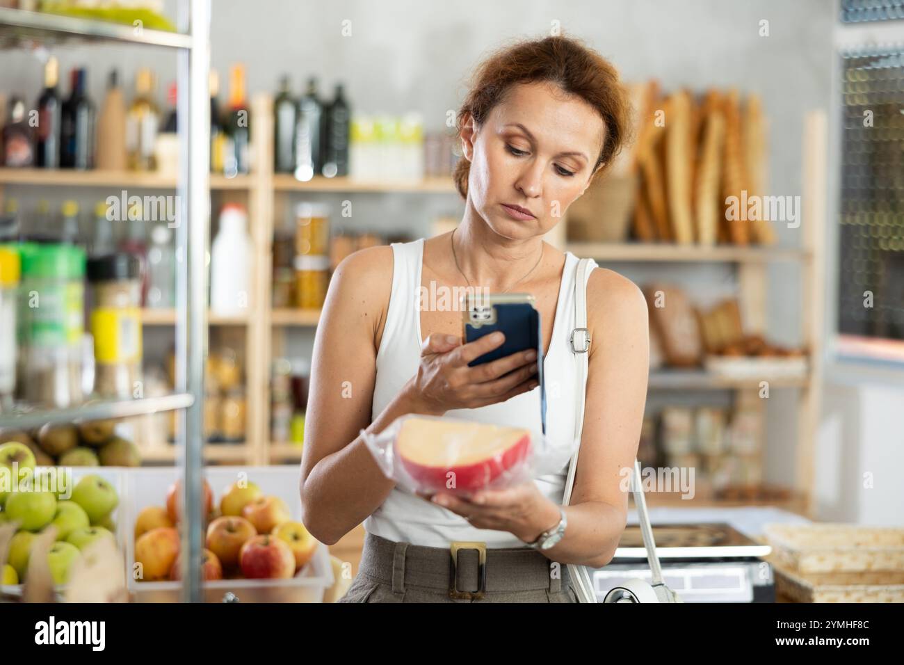 Female shopper scans QR code on cheese label using smartphone. Checking ...