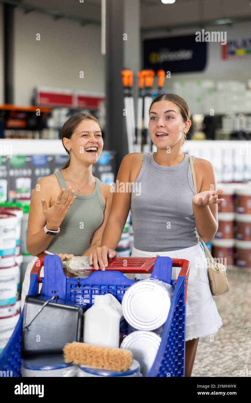 Two smiling female customers with shopping cart chooses paint tools on ...