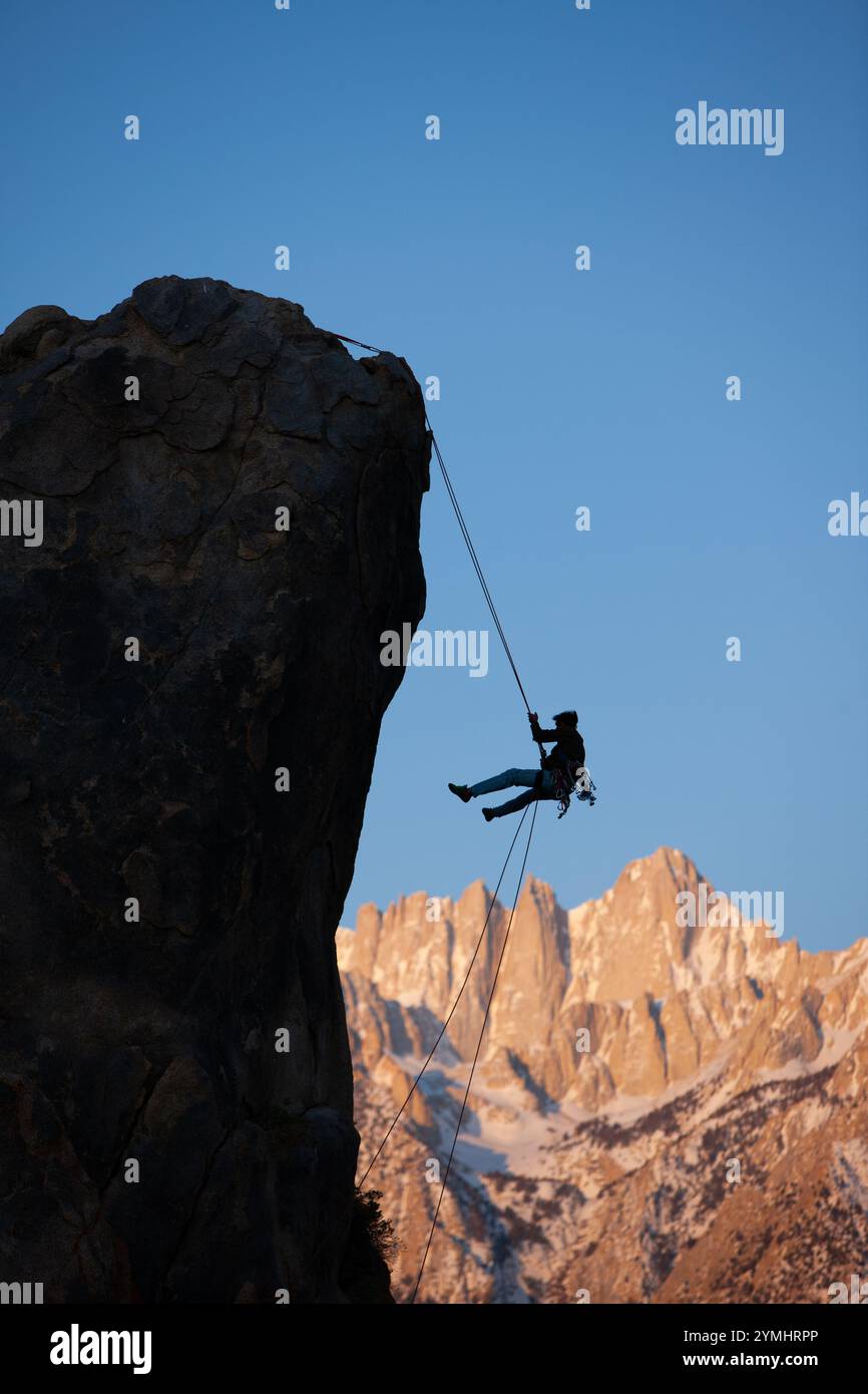 Climber rappels off of an overhanging cliff as sunrise light bathes ...