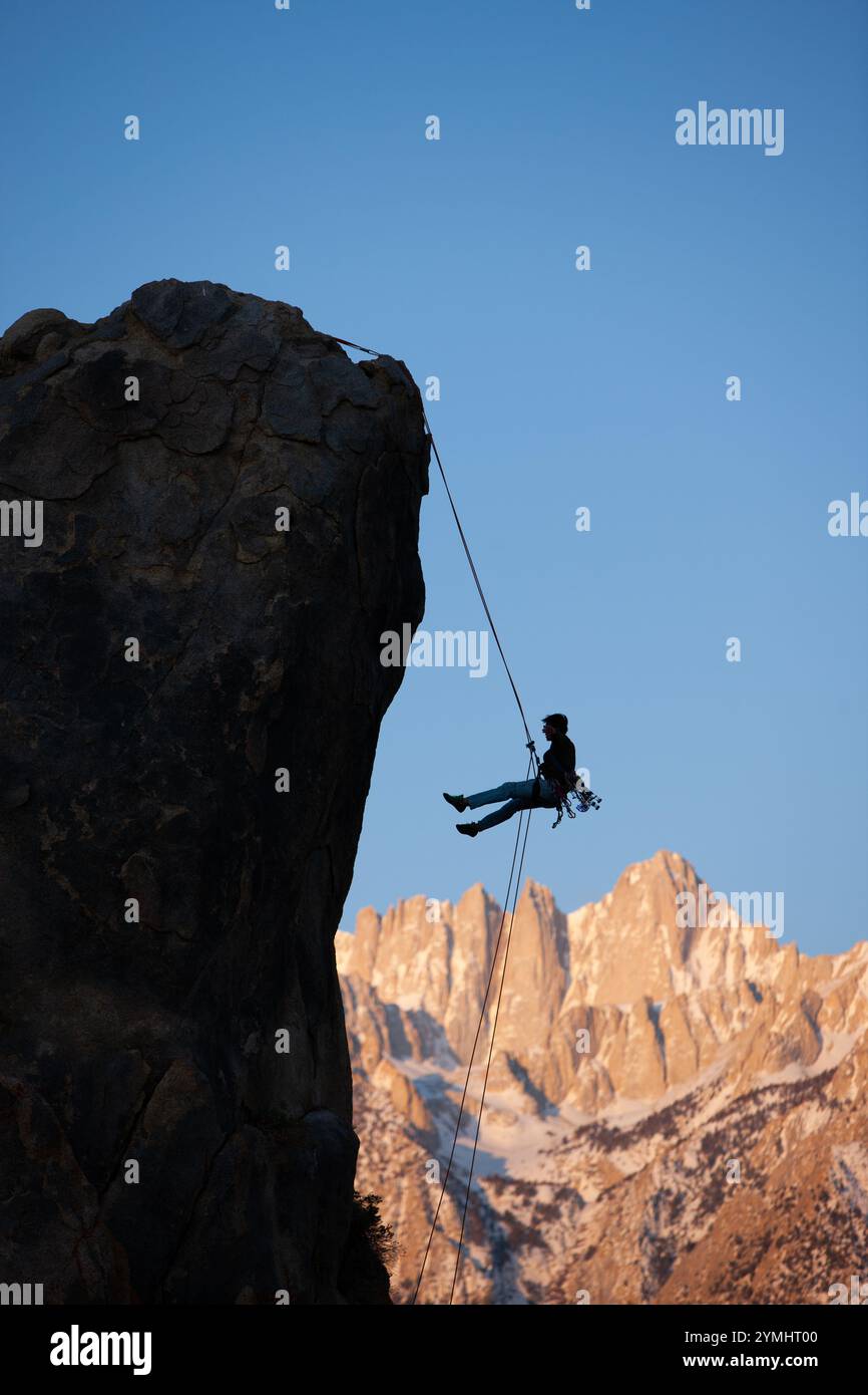 Climber rappels off of an overhanging cliff as sunrise light bathes ...
