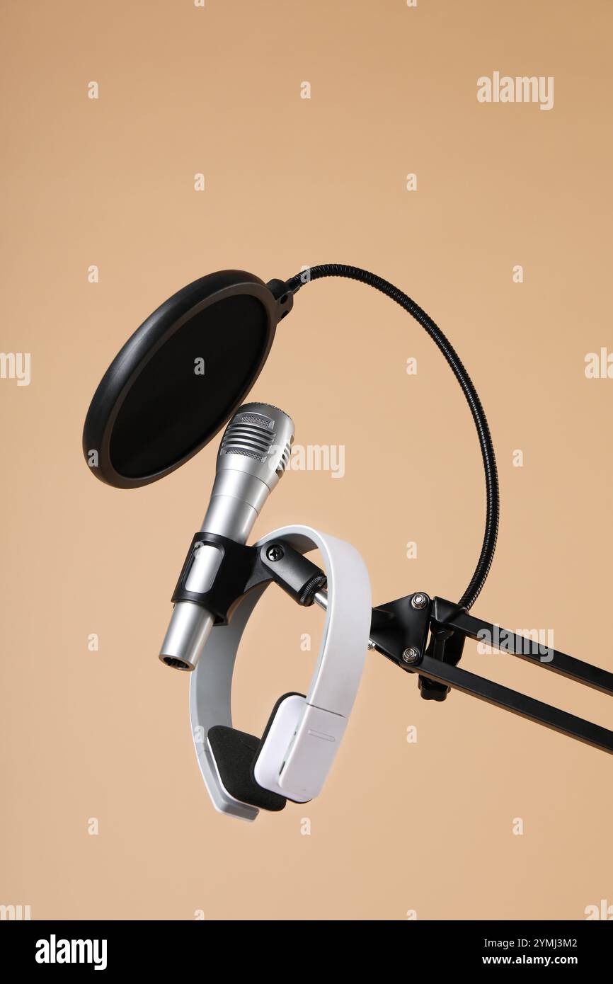 Stand with microphone, headphones and pop filter on beige background ...