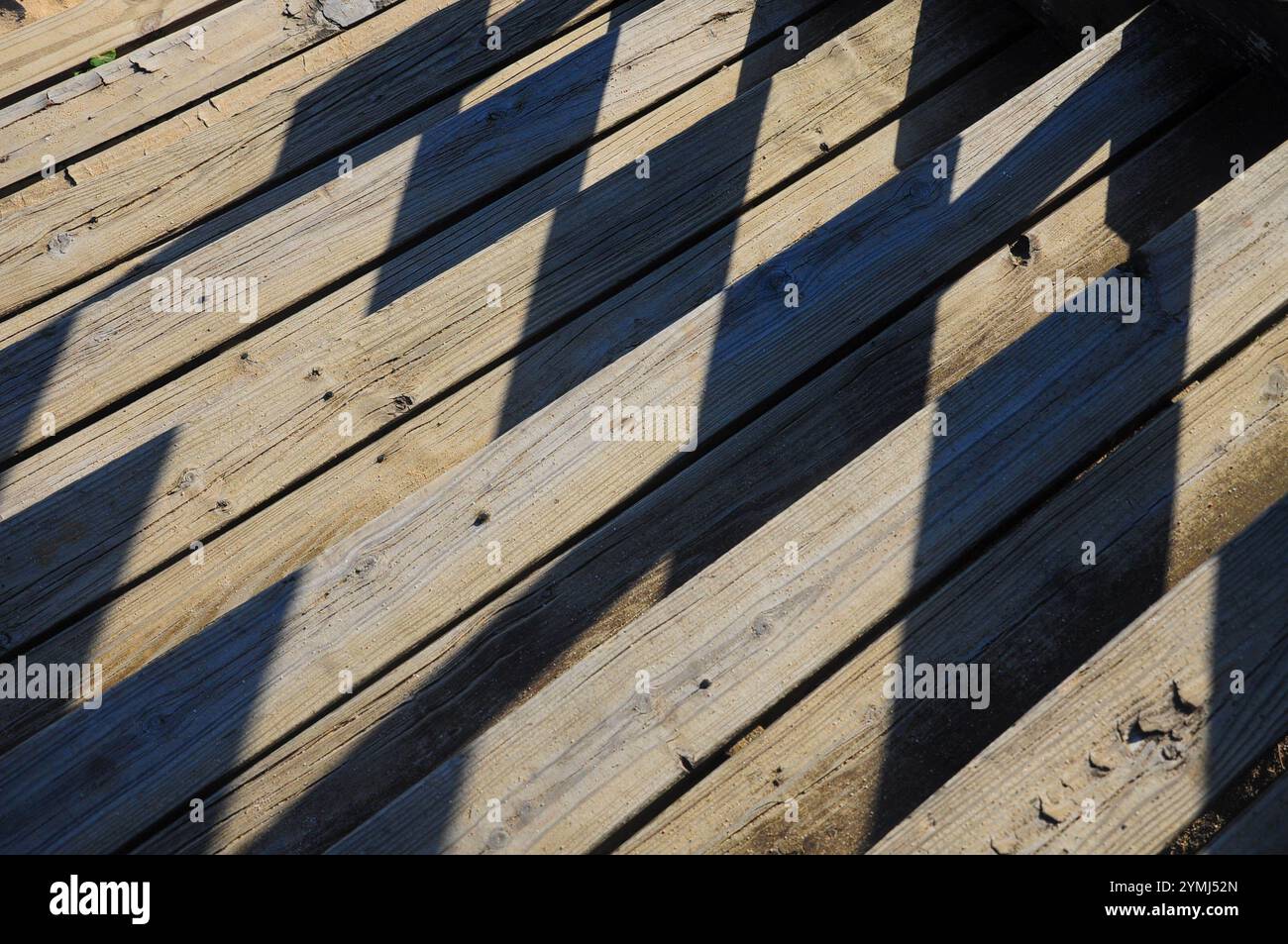 Diagonal shadows on rustic wood planks form a striking geometric ...