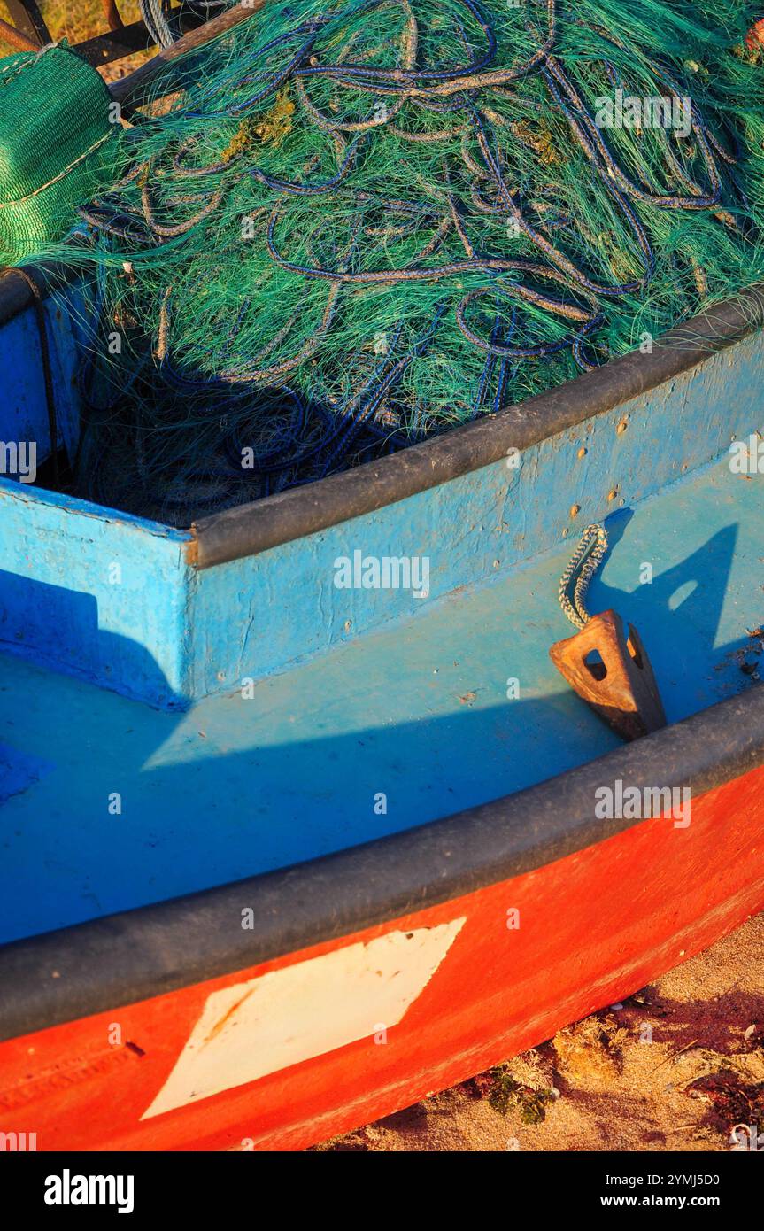 Colorful fishing boat and nets casting shadows on sandy beach under ...