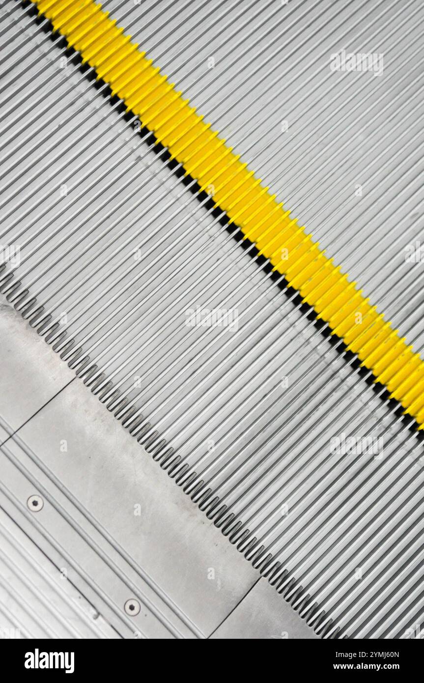 Modern escalator close-up with yellow safety markings on metallic steps ...