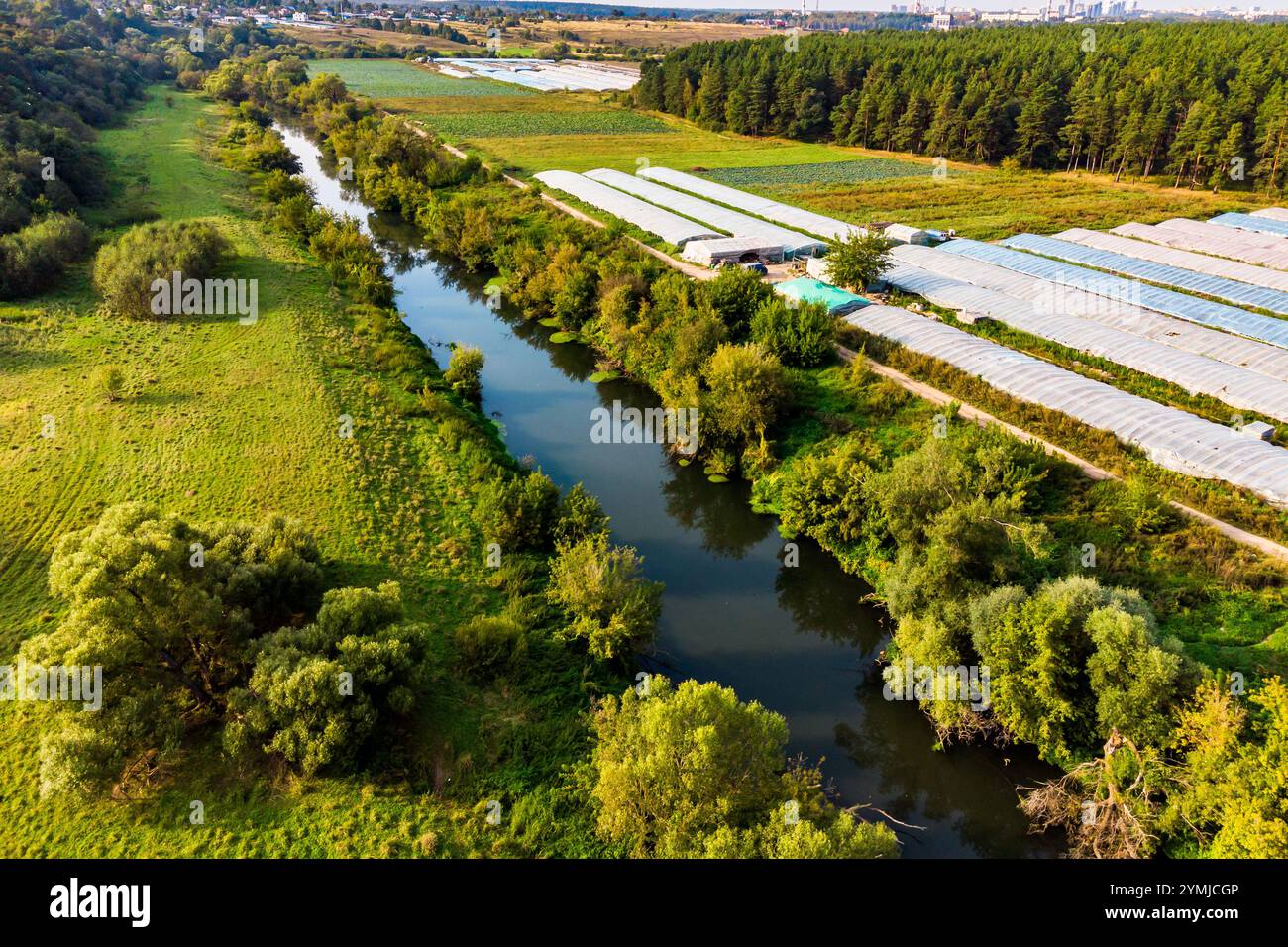Farm greenhouses in a field across a river, aerial view of a rural ...