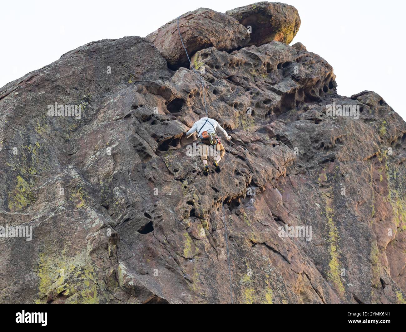 Adventurous young male rock climber ascending the sandstone rock face ...