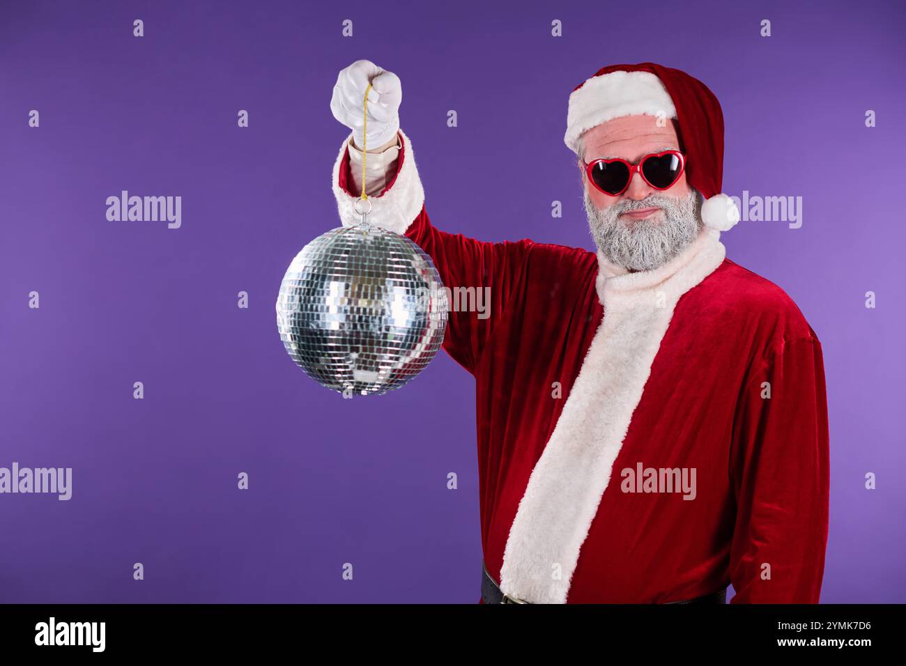Santa Claus standing against purple background holding a shiny silver ...