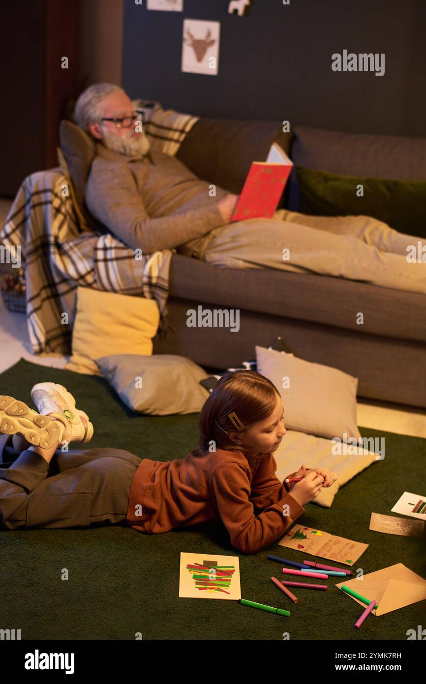 Senior man relaxing on couch reading book with child lying on floor ...