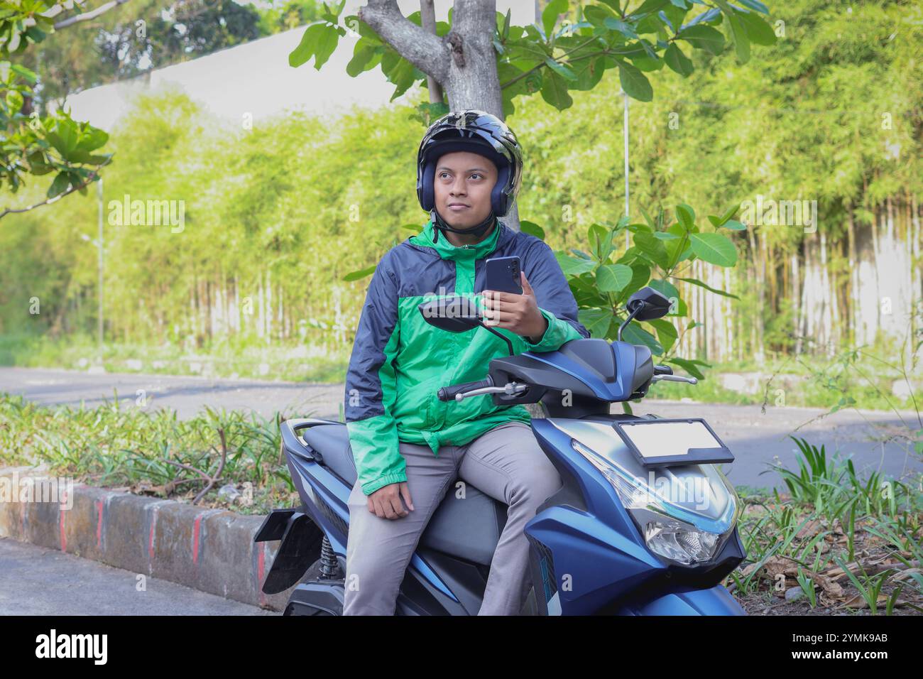 Online taxi rider wearing green jacket and helmet, riding motorcycle ...