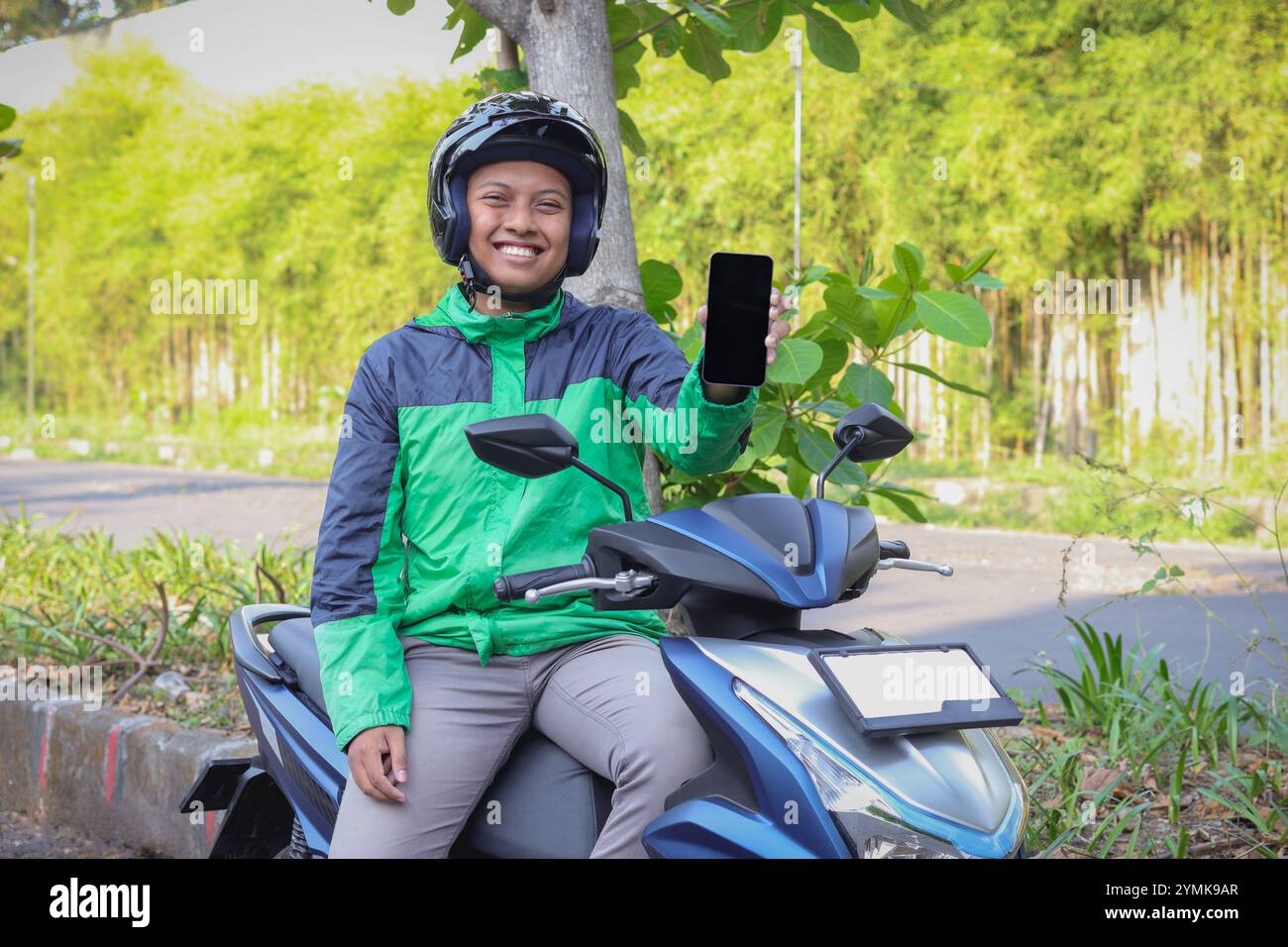 Online taxi rider wearing green jacket and helmet, riding motorcycle ...