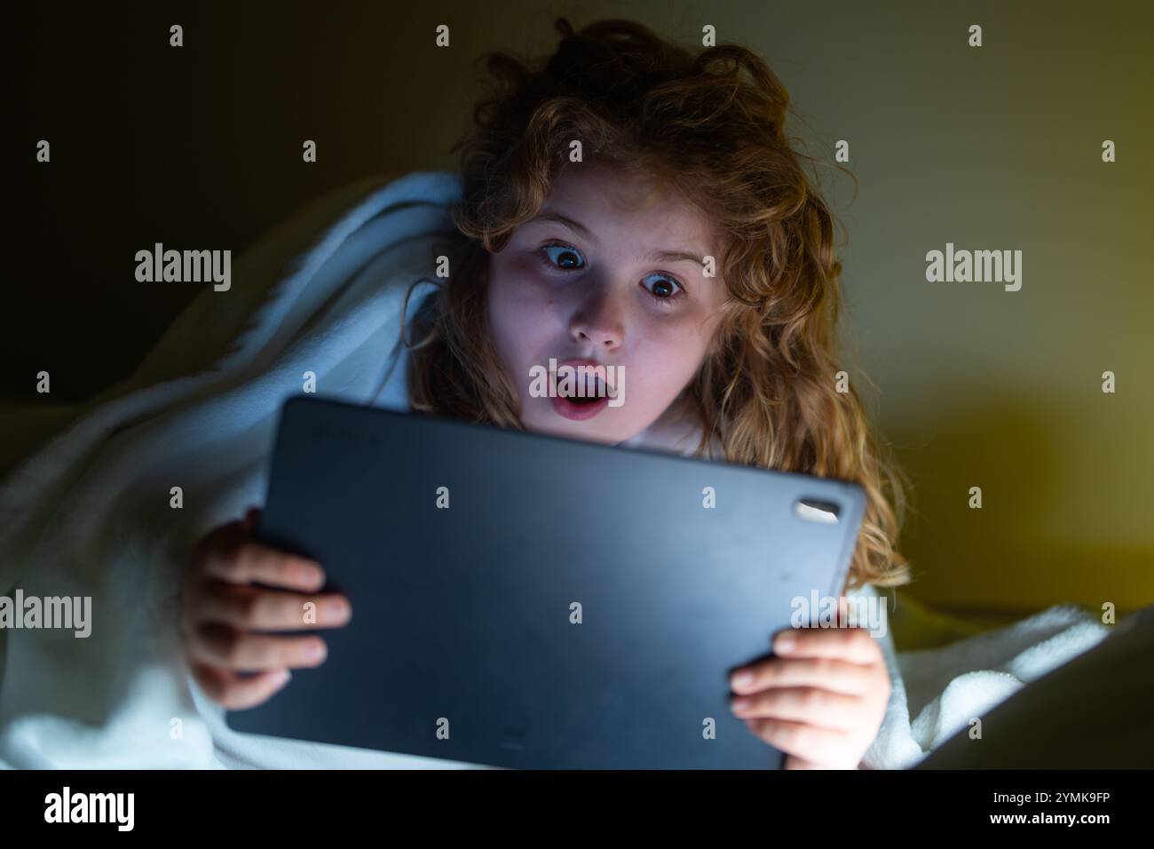 Child using Tablet in bed at night. Kid in pajamas using tablet before ...