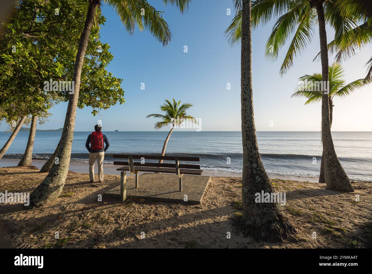 Standing facing the Pacific Ocean a backpacker is framed, on a beach ...