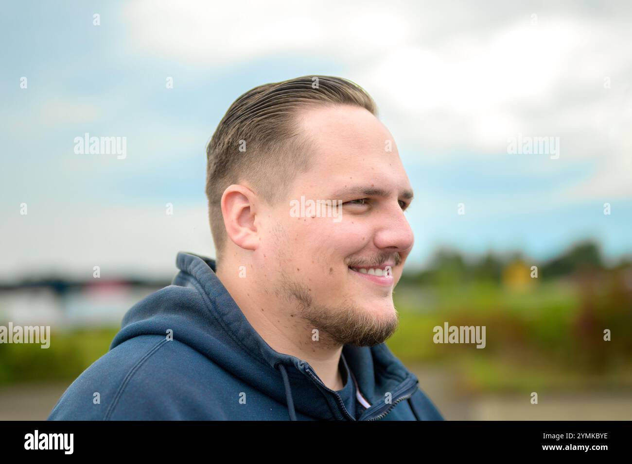 A side profile of a smiling man wearing a dark hoodie, showcasing his ...