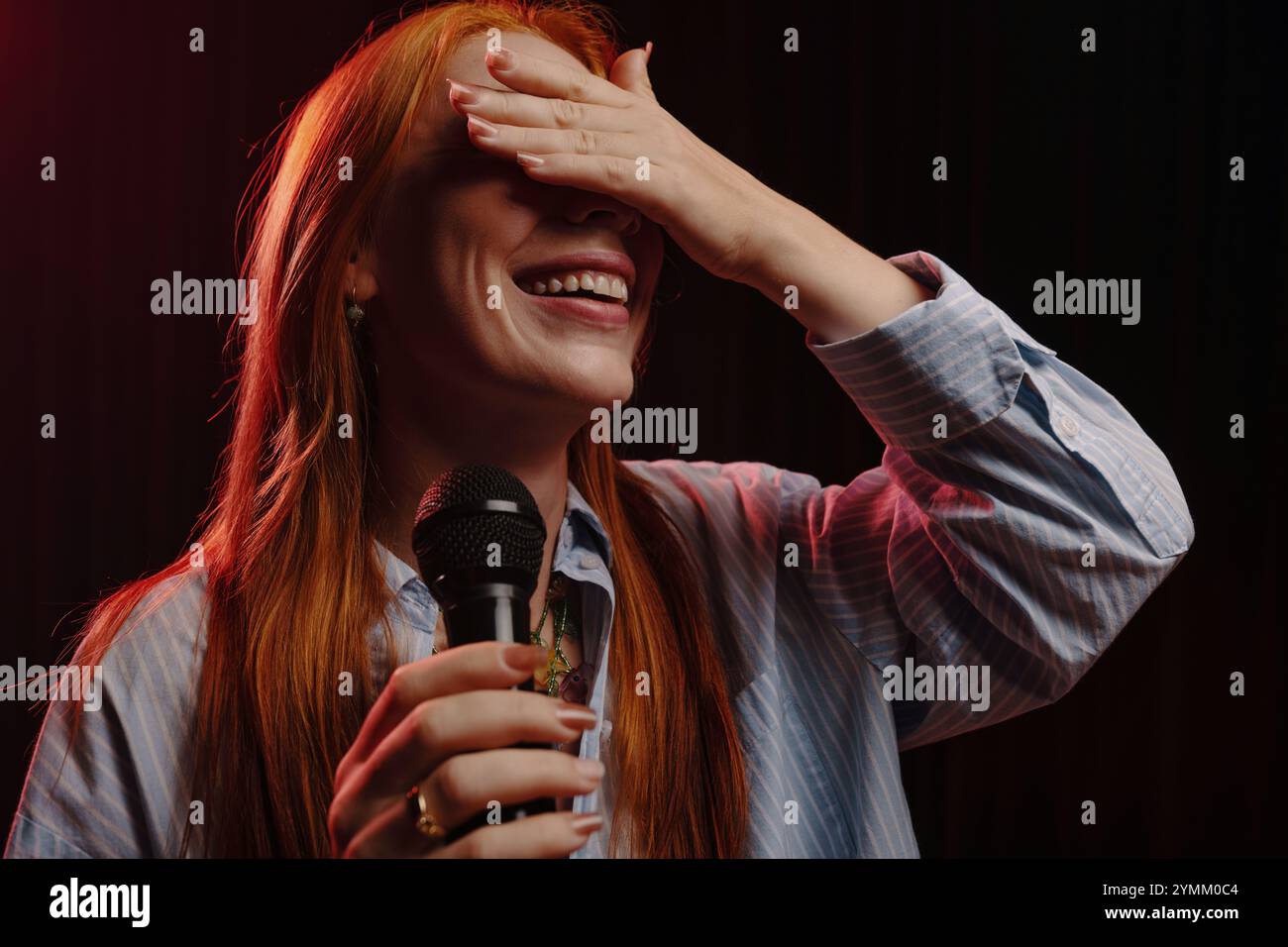 Laughing Woman Holding Microphone and Covering Face Stock Photo - Alamy