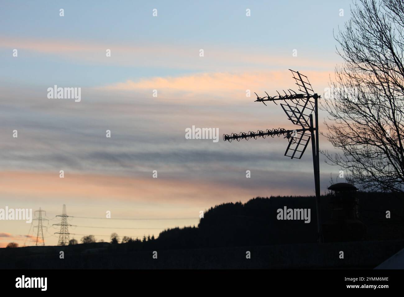 A photograph of a tv aerial on a roof with electricity pylons in the ...