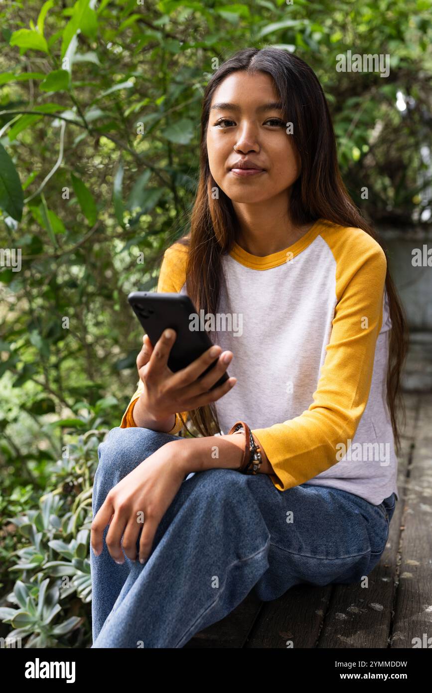 Sitting outdoors, asian female teenager holding smartphone and ...