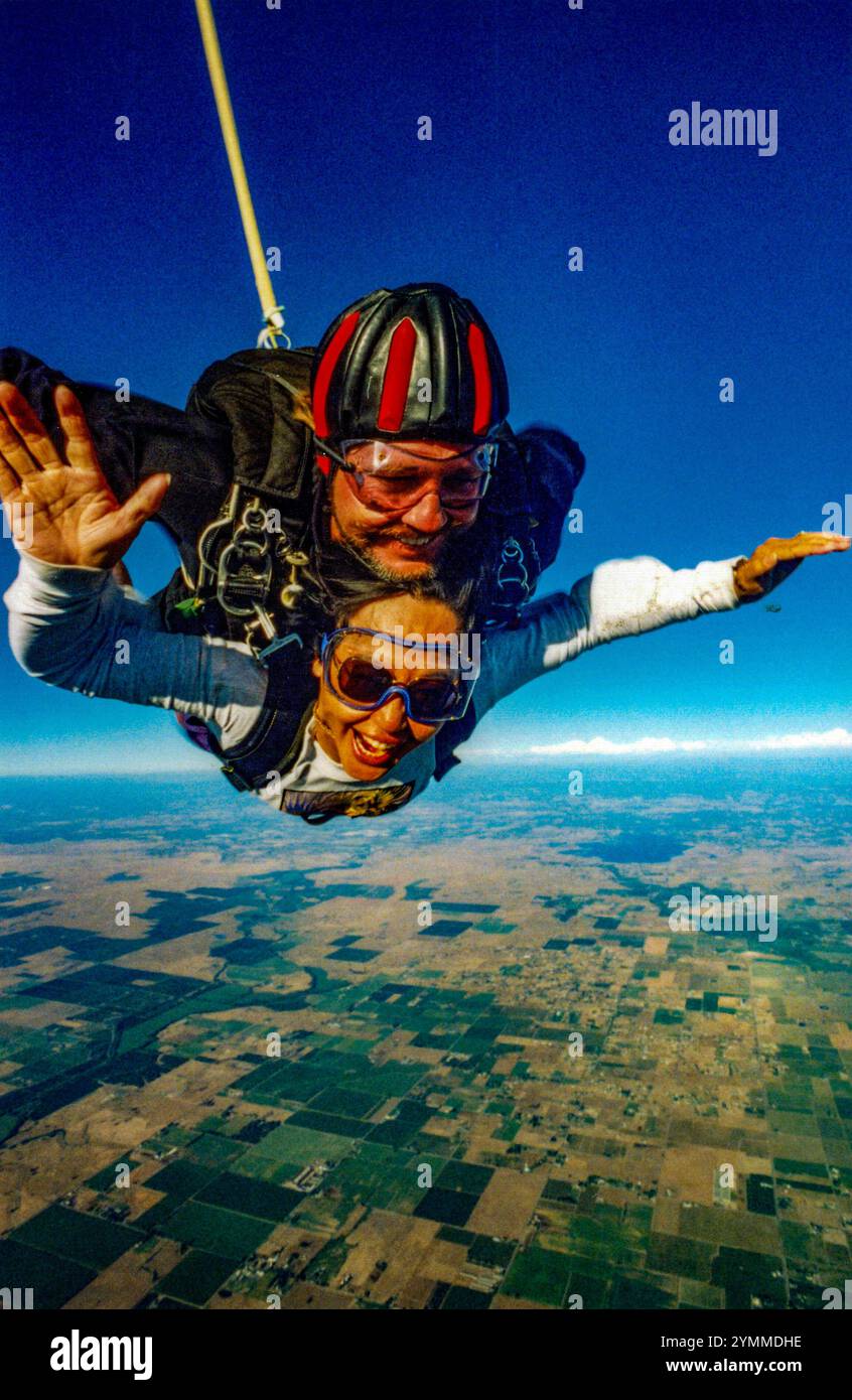 Two skydivers are smiling while doing a tandem jump, soaring high above ...