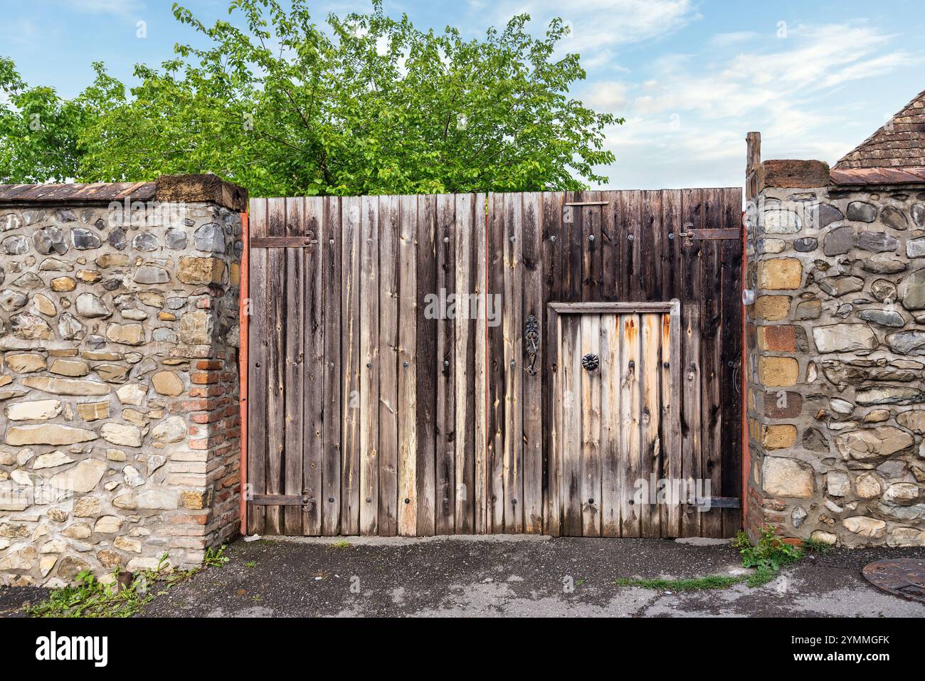 A rustic wooden gate stands tall between aged stone walls, with a ...