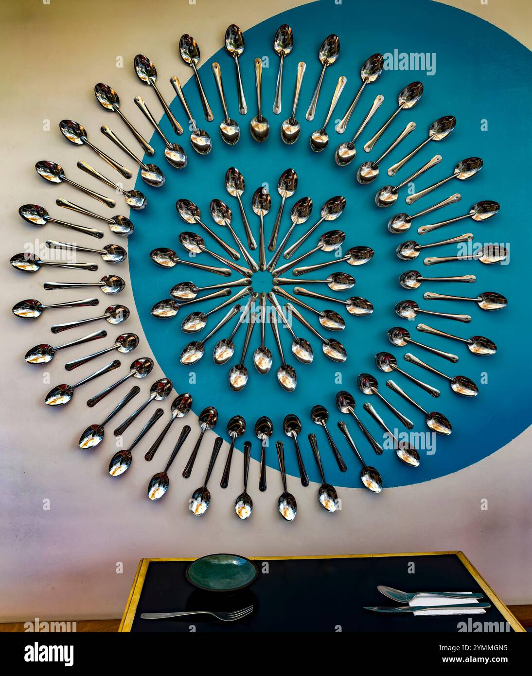 Many spoons are forming a spiral shape on a teal and white wall ...