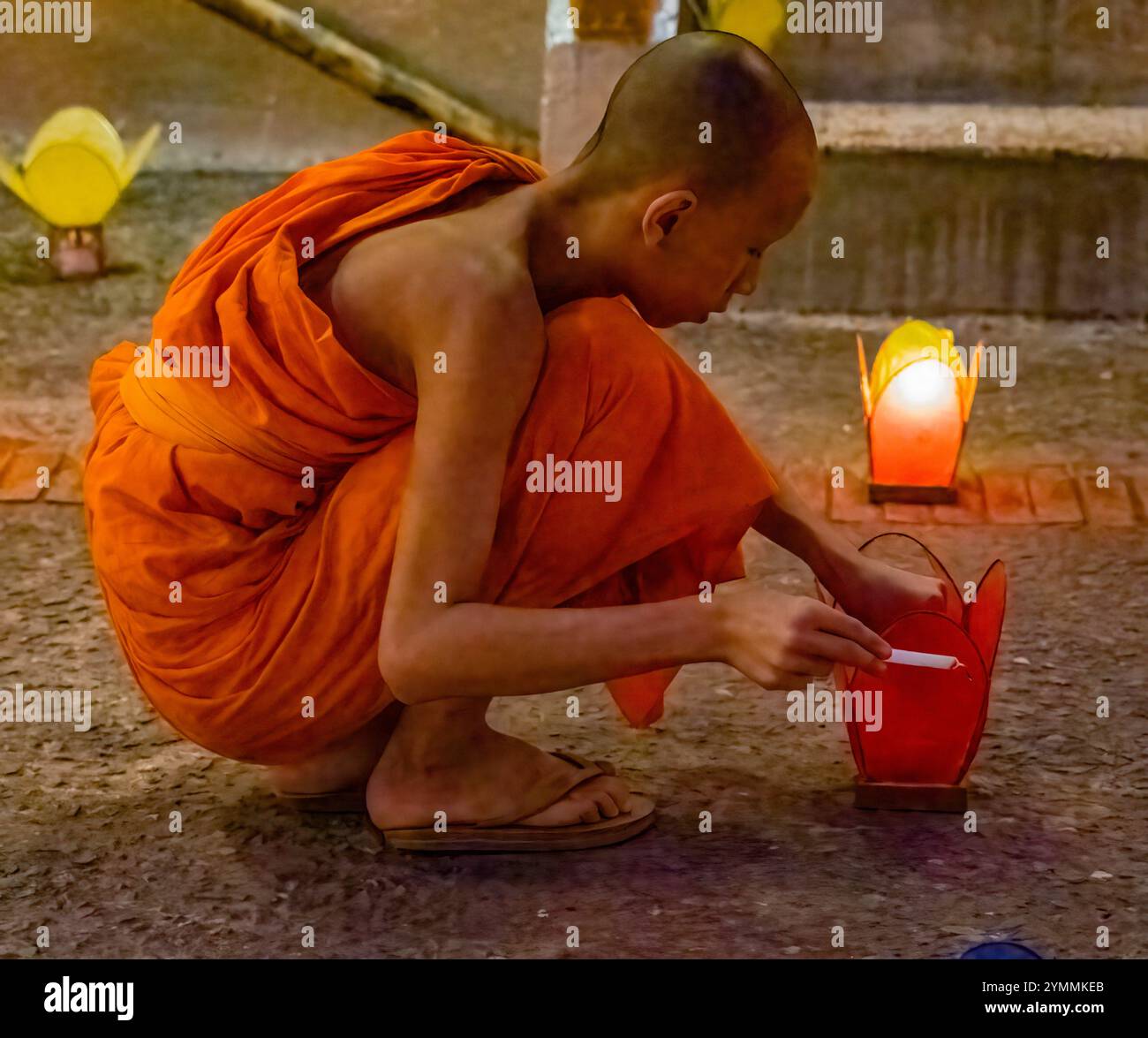 Young buddhist monk wearing orange robes lighting candles during a ...