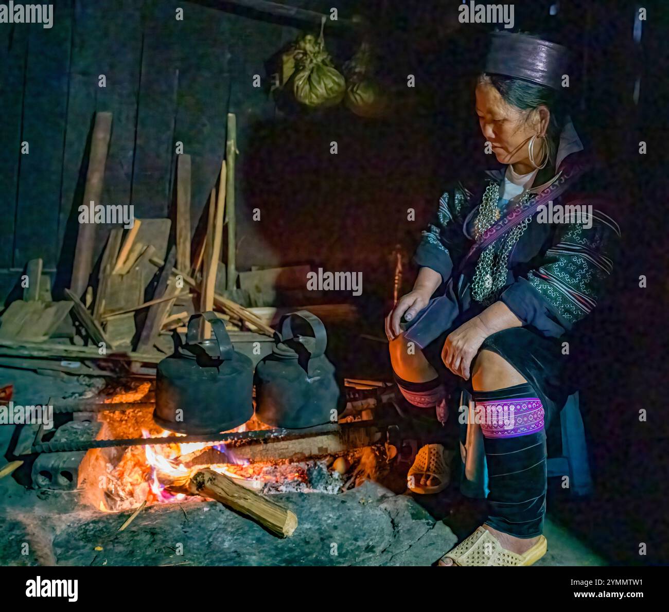 Elderly black hmong woman sitting next to a fire, heating water in ...