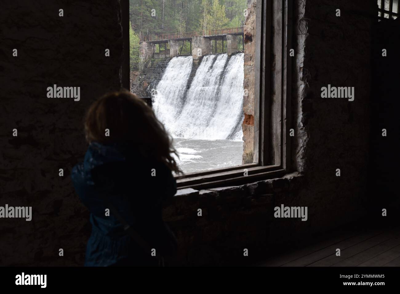 A person gazes at a cascading waterfall through an old stone window ...