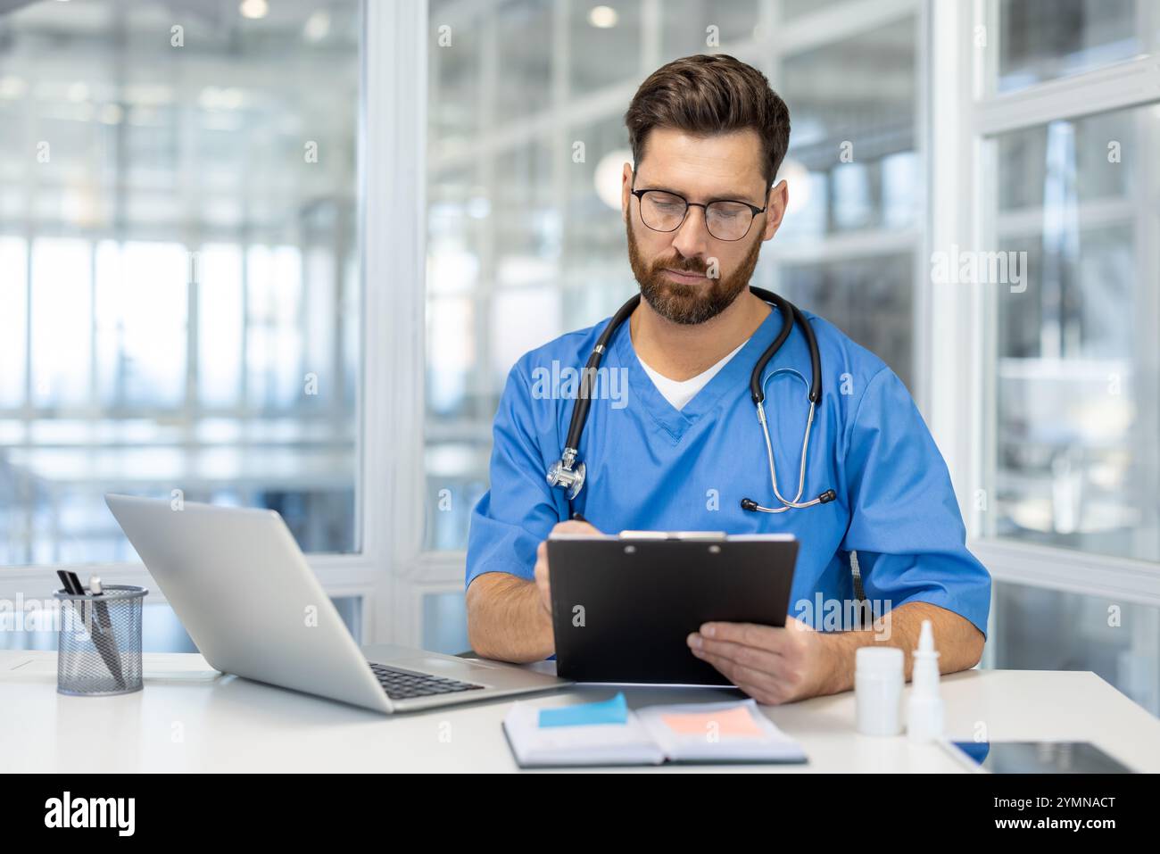 Man doctor wearing blue scrubs and glasses reviewing documents with ...