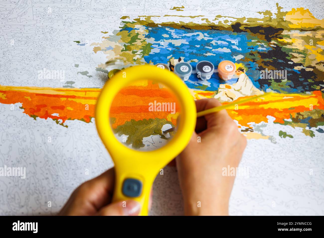 A woman paints a picture by numbers while looking through a magnifying ...